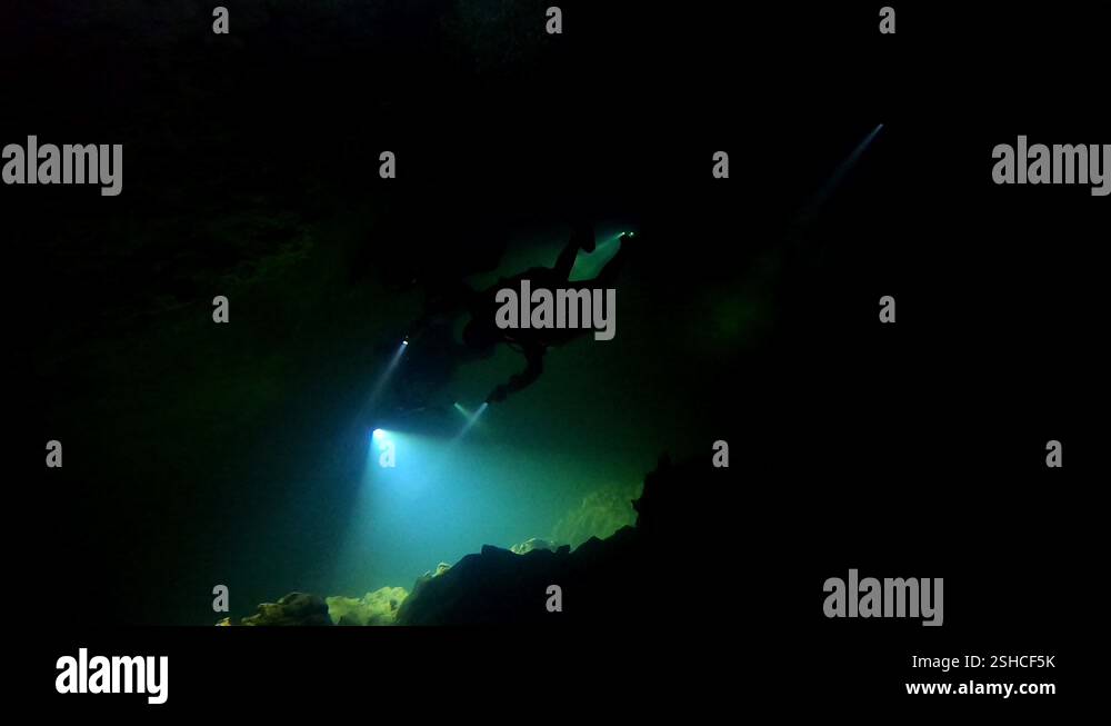 Cave divers exploring a cave with torches close to a silt layer at the ...