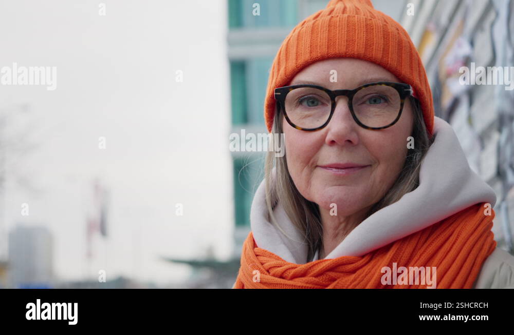 Urban style mature female standing near fence wall covered with posters ...