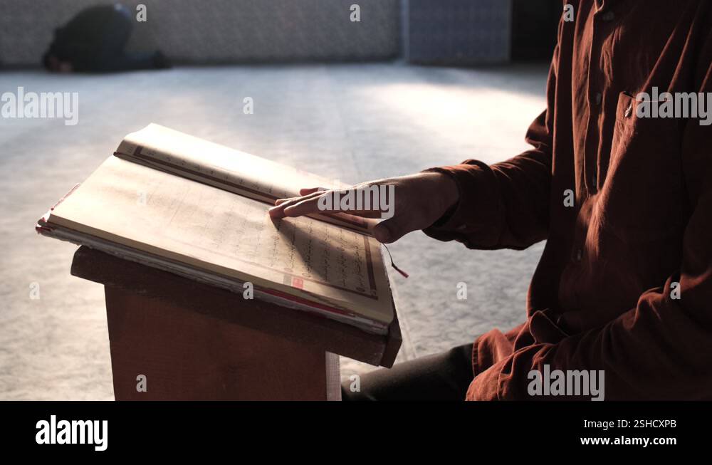 Side view of a man reading the Islamic religious book Quran with his ...