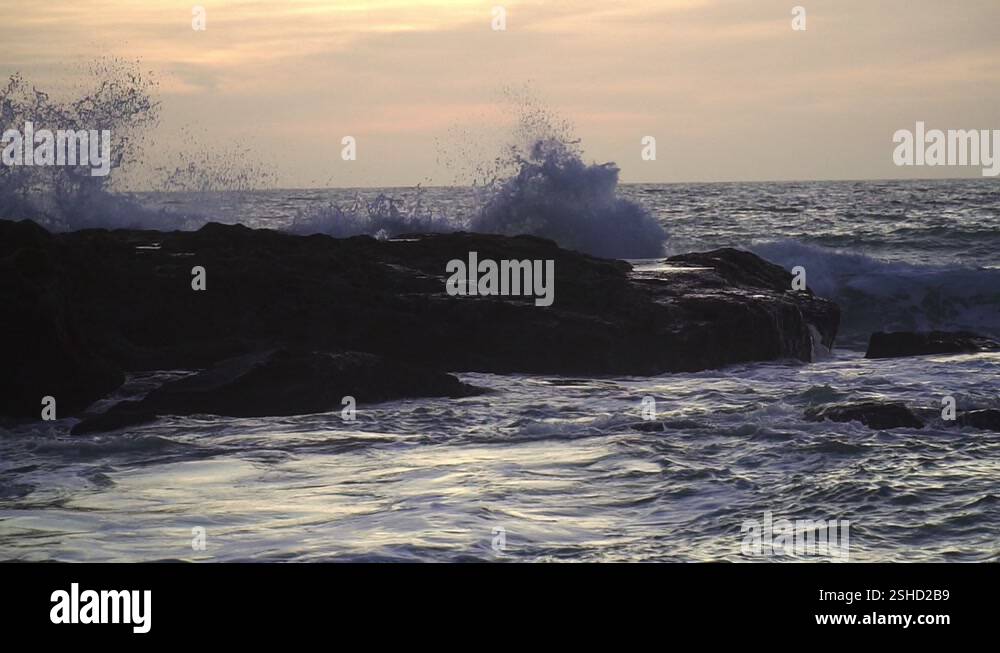 Rough sea with waves breaking against rocks in the sea, in a sunset ...