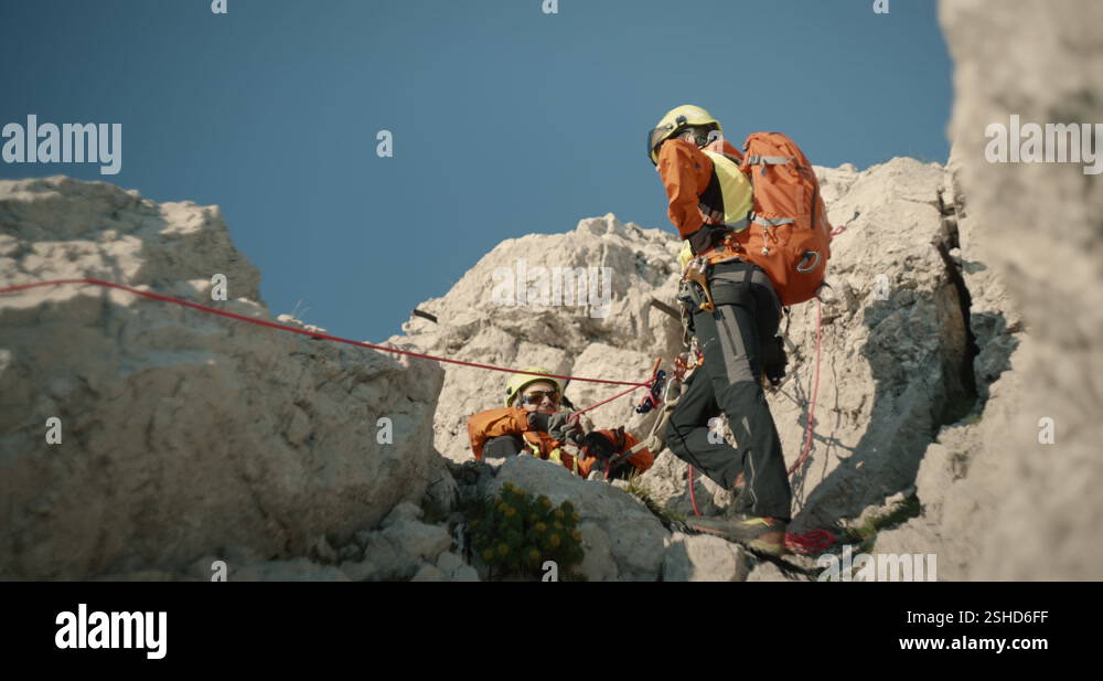 Lower perspective of two hikers tieing rope for a secure descent from ...