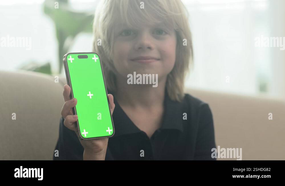Smiling blonde boy showing phone with chroma key green screen and ...