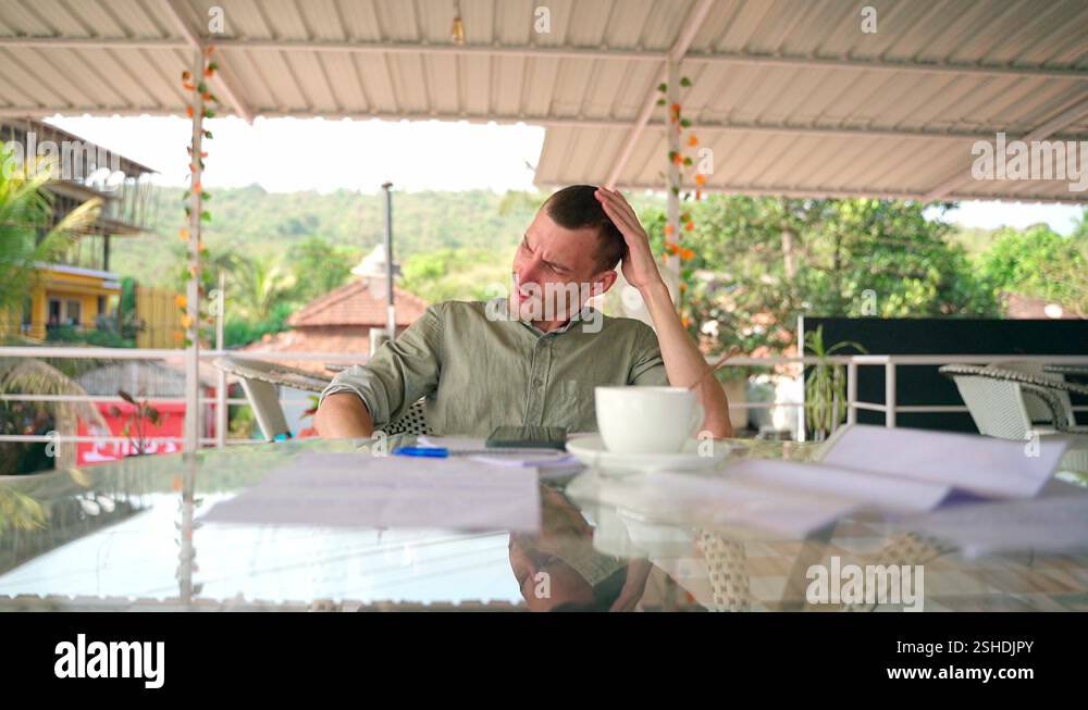 The man nervously throws the phone on the table, rubbing his head with ...
