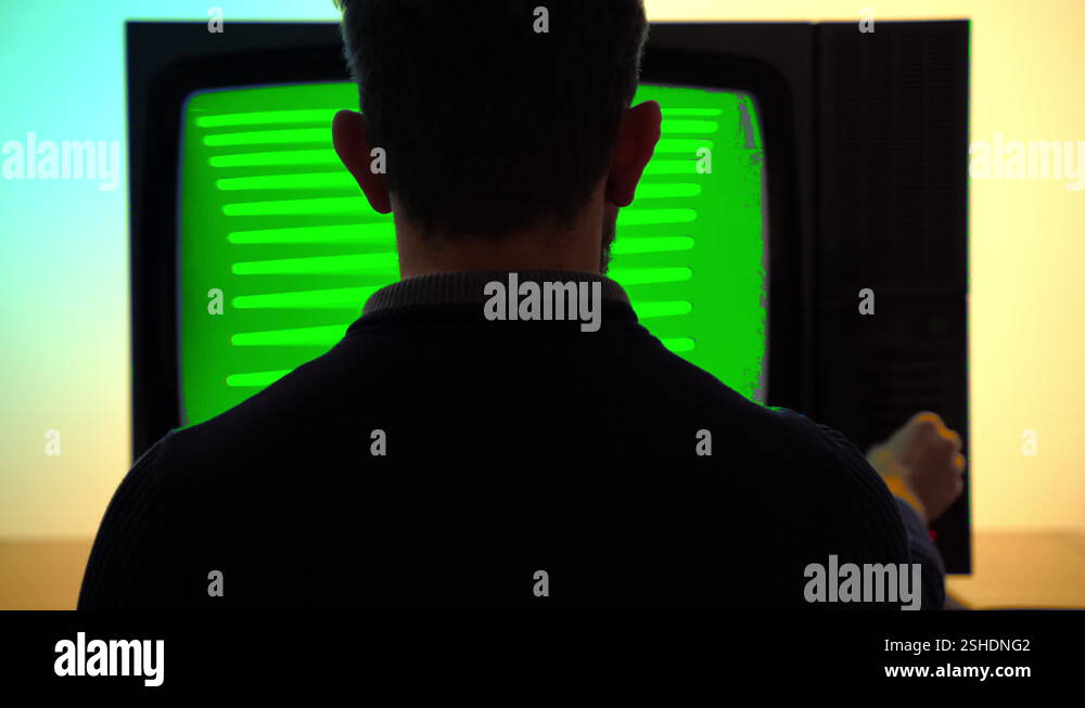 Back view shot of male person sitting in front of vintage TV with ...