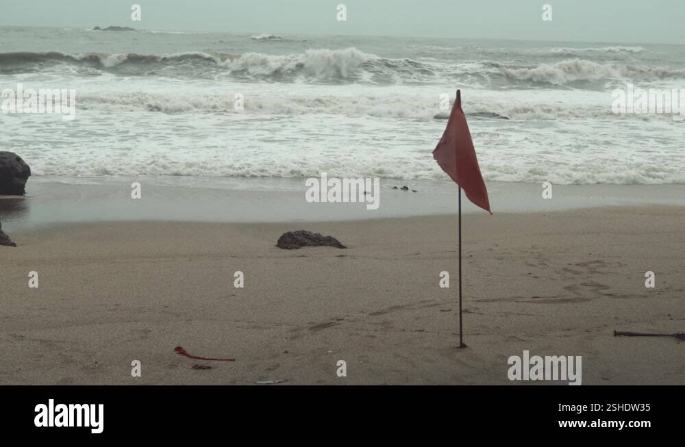 Beach and lifeguard warning red flag stuck in the sand with waves ...