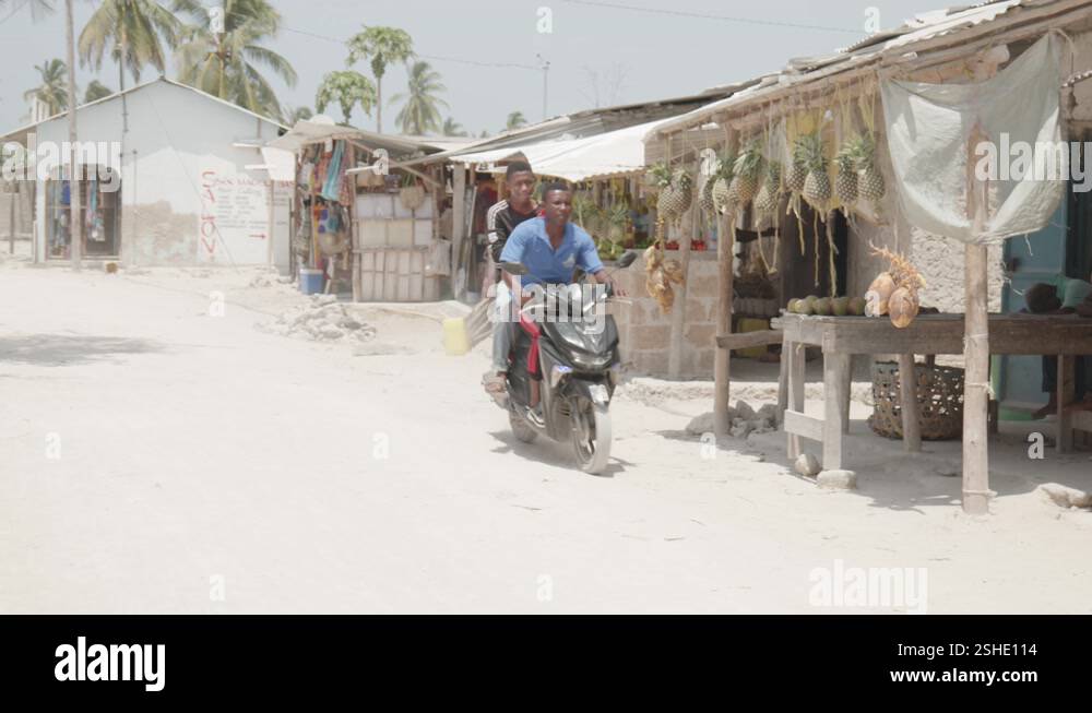 Two young black men driving on motorbike through village in Africa ...