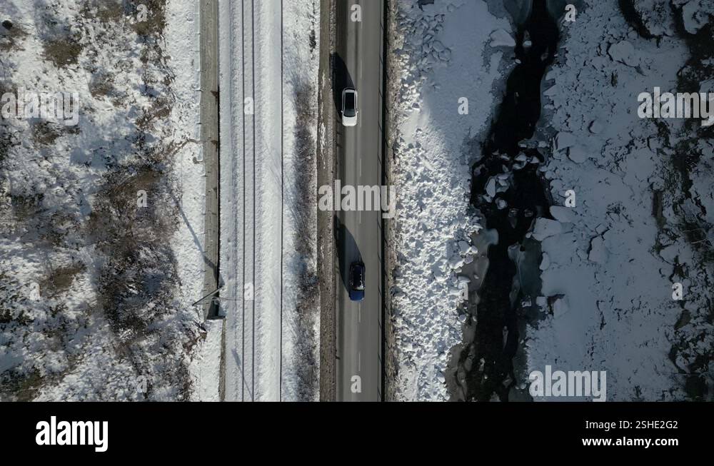 An icy railroad track, a road with cars and a frozen creek bed. One car ...