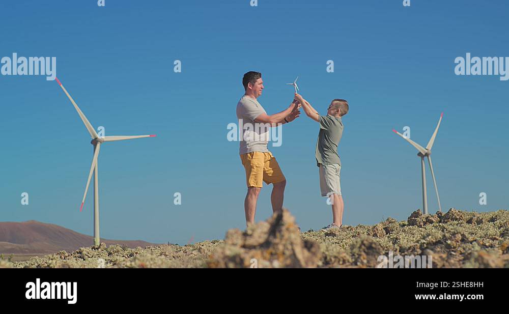 Happy father and son on looking at wind energy turbine sat wind farm ...