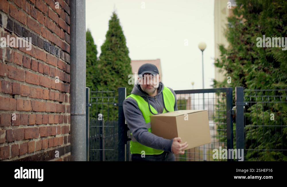 Cheerful handsome postman in uniform opens gate to delivering big ...