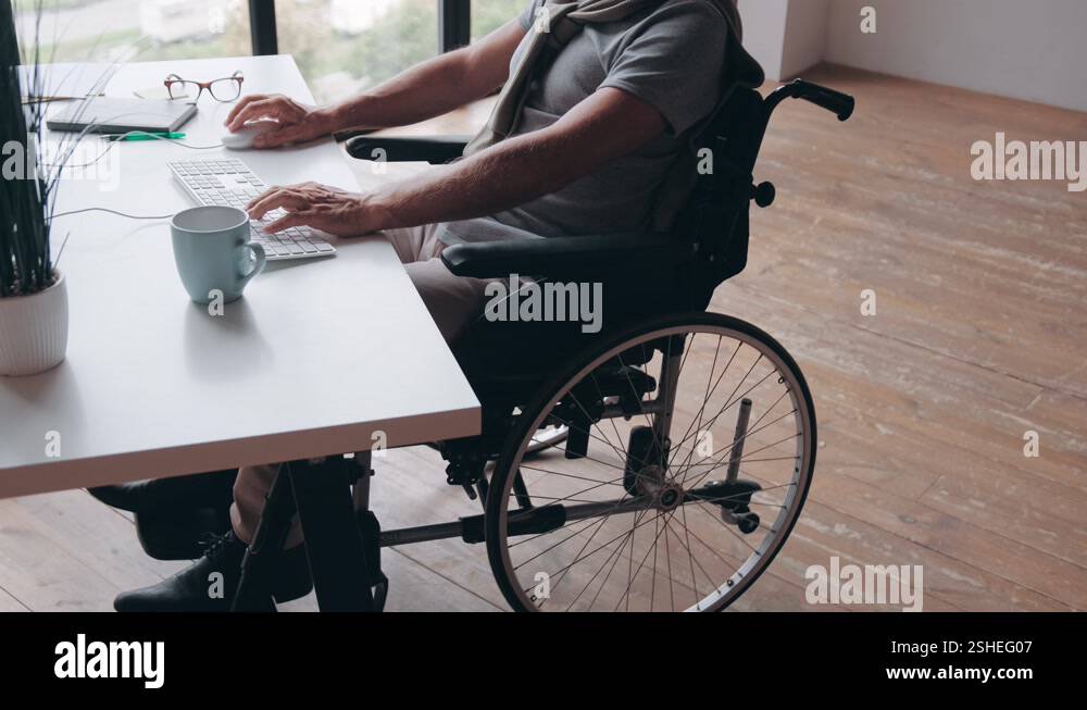 disabled man sitting in wheelchair at the table in front of computer ...