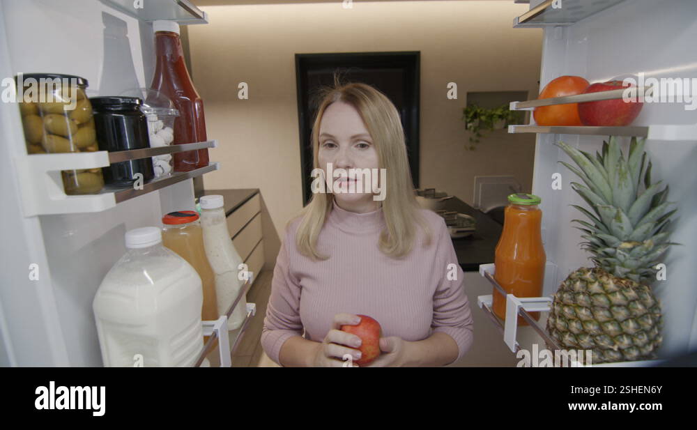 The woman takes an apple from the refrigerator. Light snack, view from ...