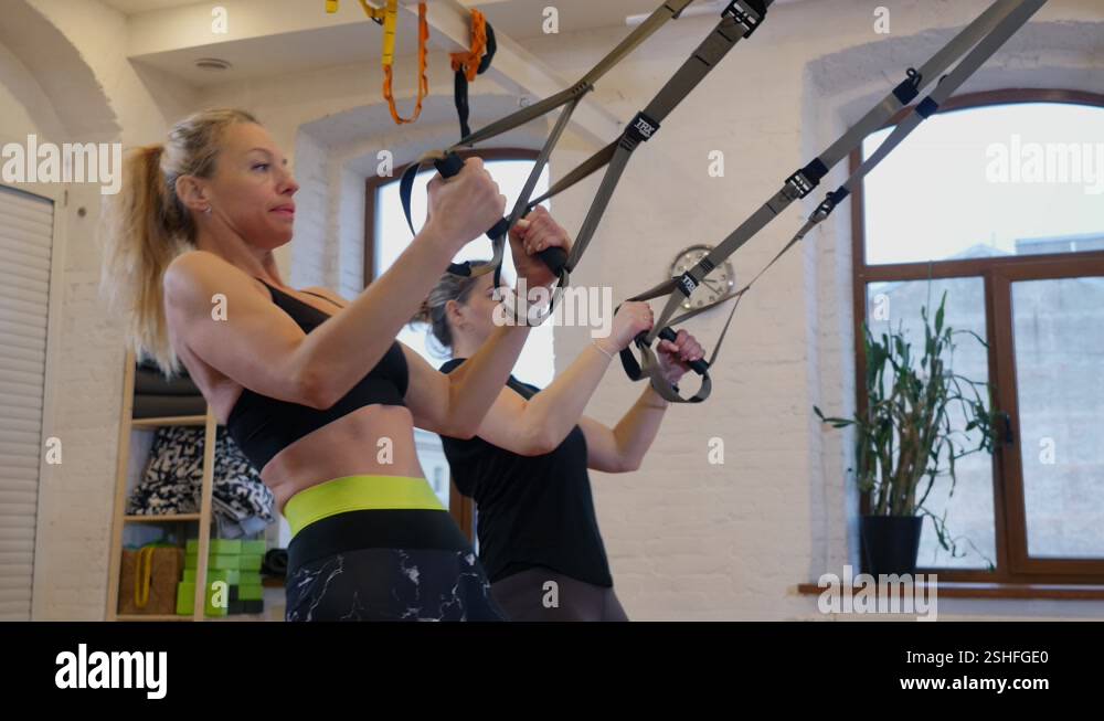 Fitness coach and young woman doing pull-ups with trx loops indoors ...