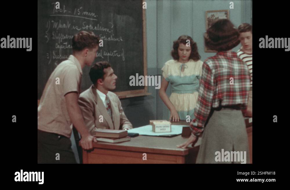 1940s: Kids in classroom around desk, boy walks to box. Hand looks ...