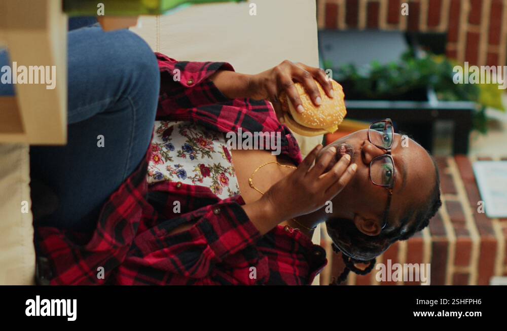 Vertical video: Young woman eating cheeseburger with fries and beer ...