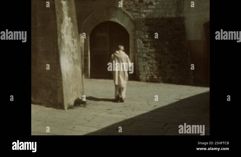 1950s: Monk carrying a book walks through a courtyard and enters a pair ...