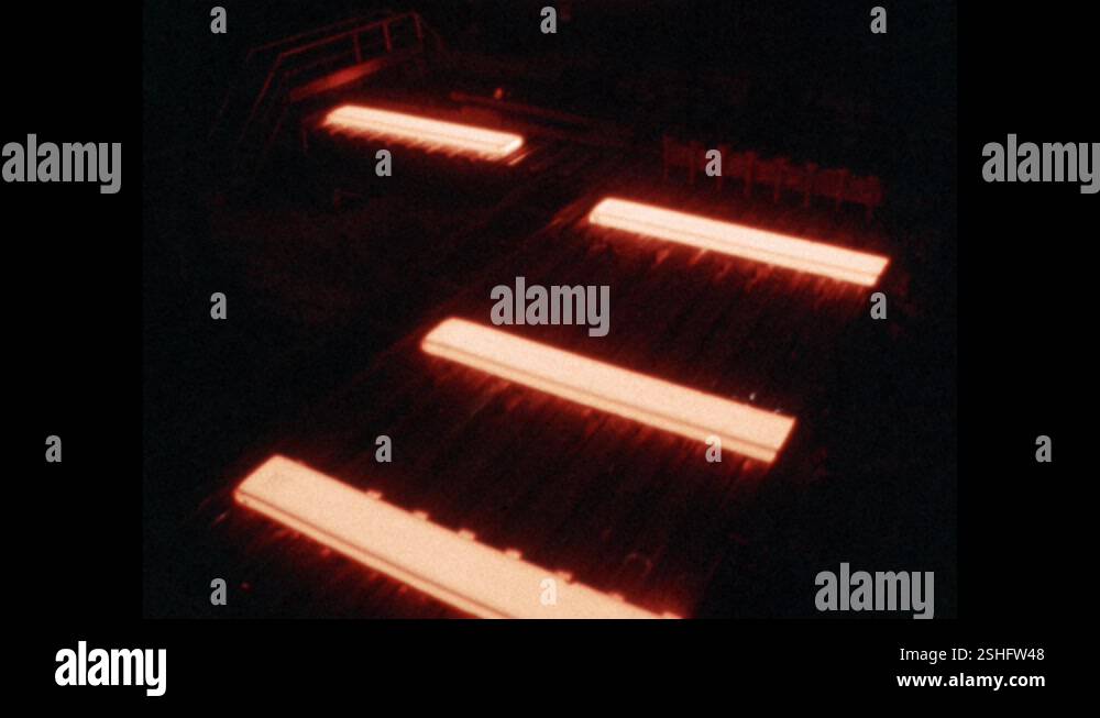 1970s: Molten steel bars move along conveyor belts. Man operates sheet ...