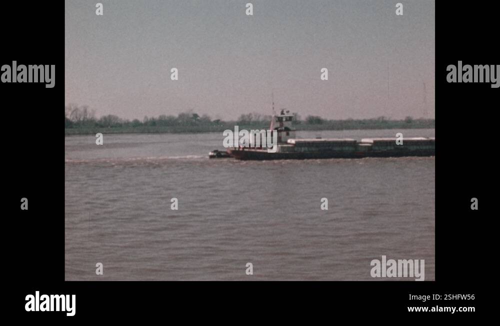 1970s: Barge moves bins of coal up river. Man operates controls and ...