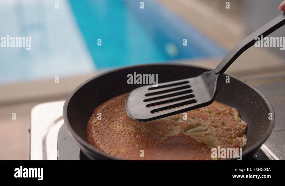 Turning a pancake in a pan. Big round pancake on induction frying pan ...