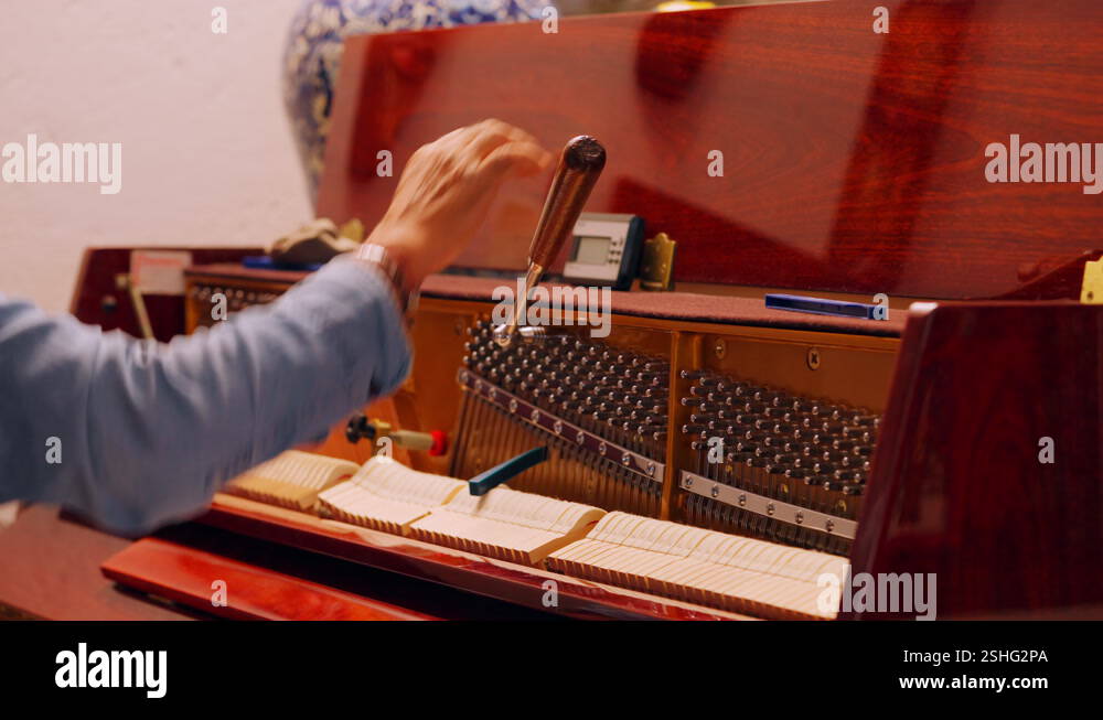 Man tuning a wooden piano, open piano with chords visible and hammer ...