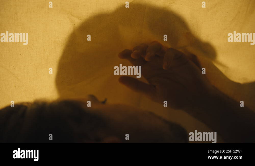 Silhouette of woman backlit on muslin while man lays on other side ...