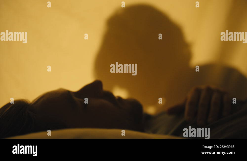 Silhouette of woman backlit on muslin while man lays on other side ...