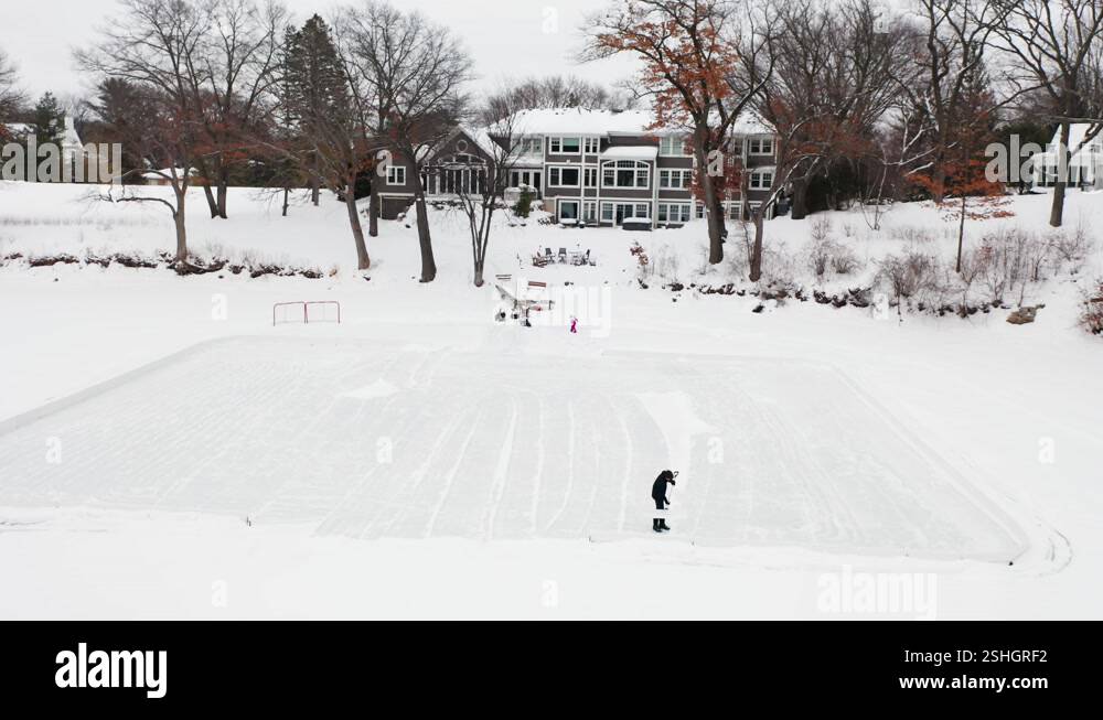 Person shoveling snow alone to make outdoor ice hockey skating rink ...