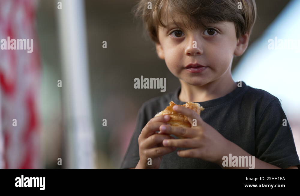 Child snacking bread outside. One small boy standing outdoors eating ...