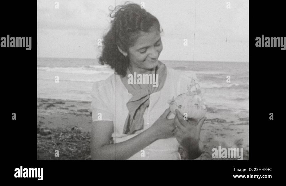 1940s: People stoop on beach. Girl holds sea shell. Boy holds goat ...