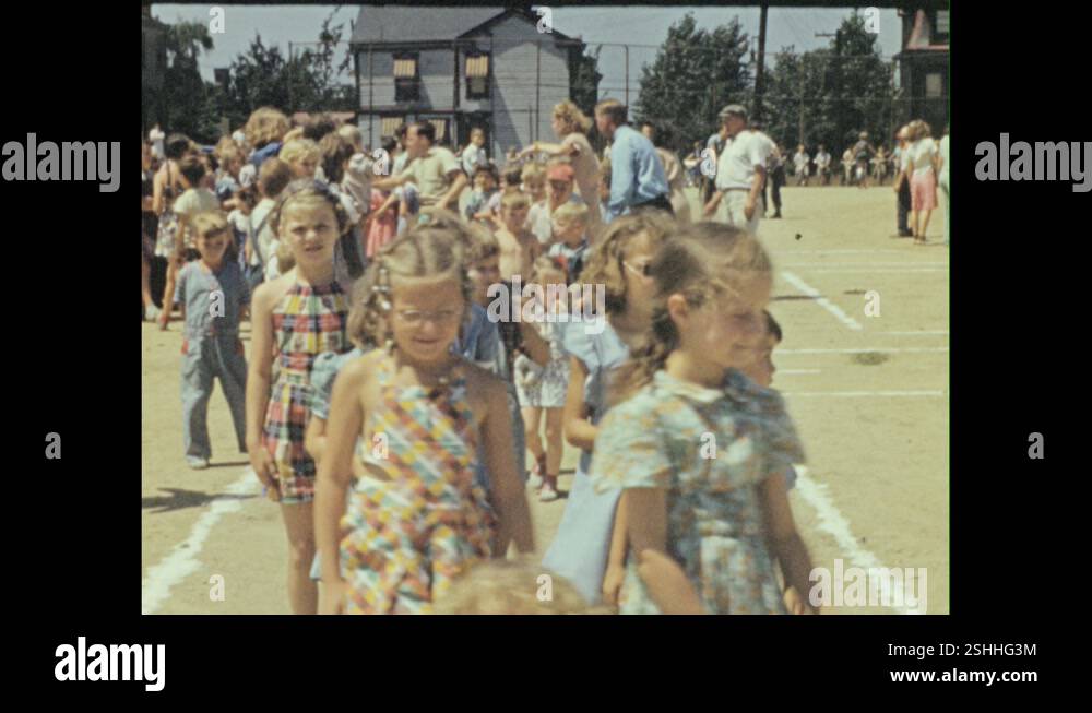 1930s: Children walk in a line on a playfield. Man talks to a group of ...
