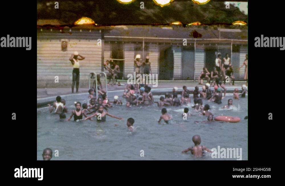 1930s: Children play, wade and splash in a swimming pool. Lifeguard ...