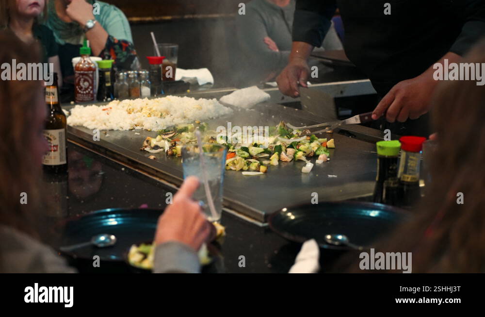 Diners sit around hibachi grill table as chef sautes and cooks large ...