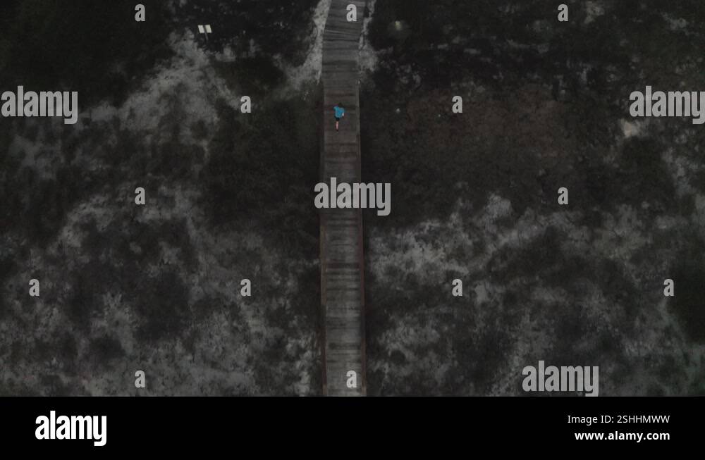 Aerial top down, man running on wooden plank boardwalk, grayscale ...