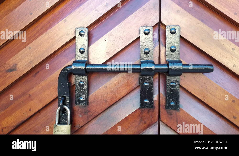 Metal security bar on a wooden double door with padlock. Black steel ...