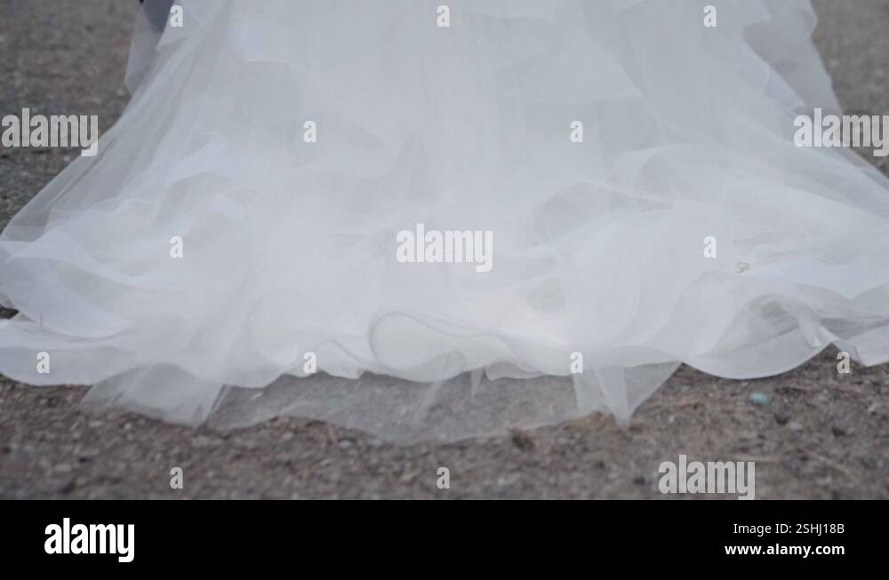 Beautiful wedding dress dragging on the floor. The groom accompanies ...