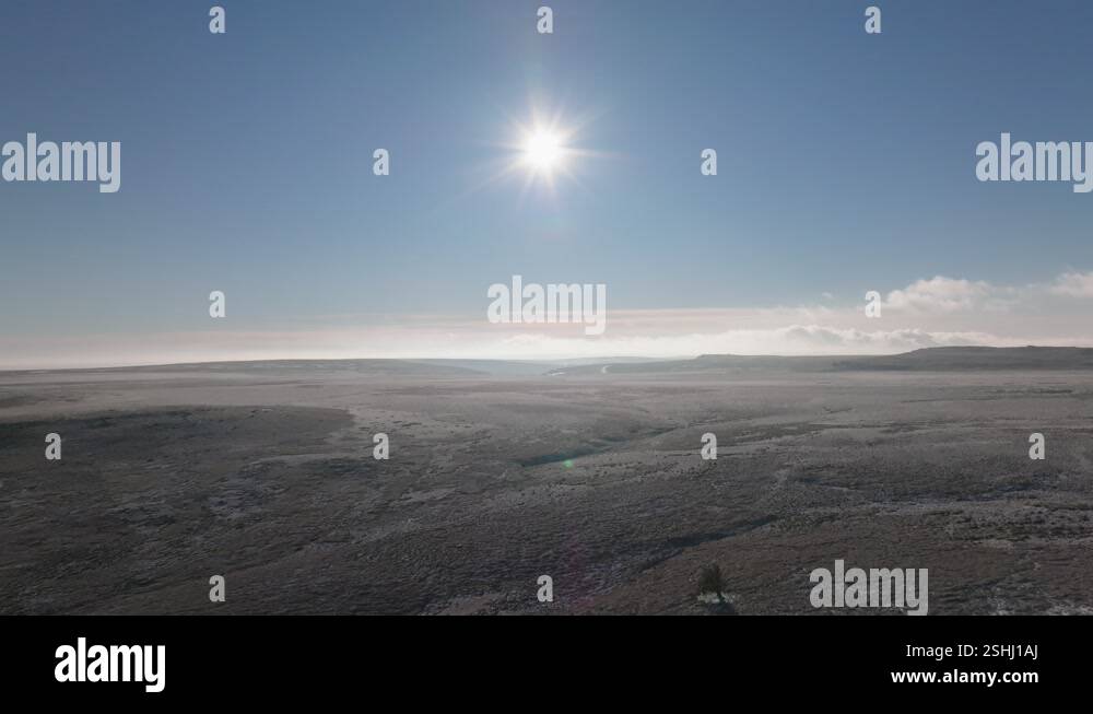 A low winter sun and blue sky over a large frozen moorland, snowy ...