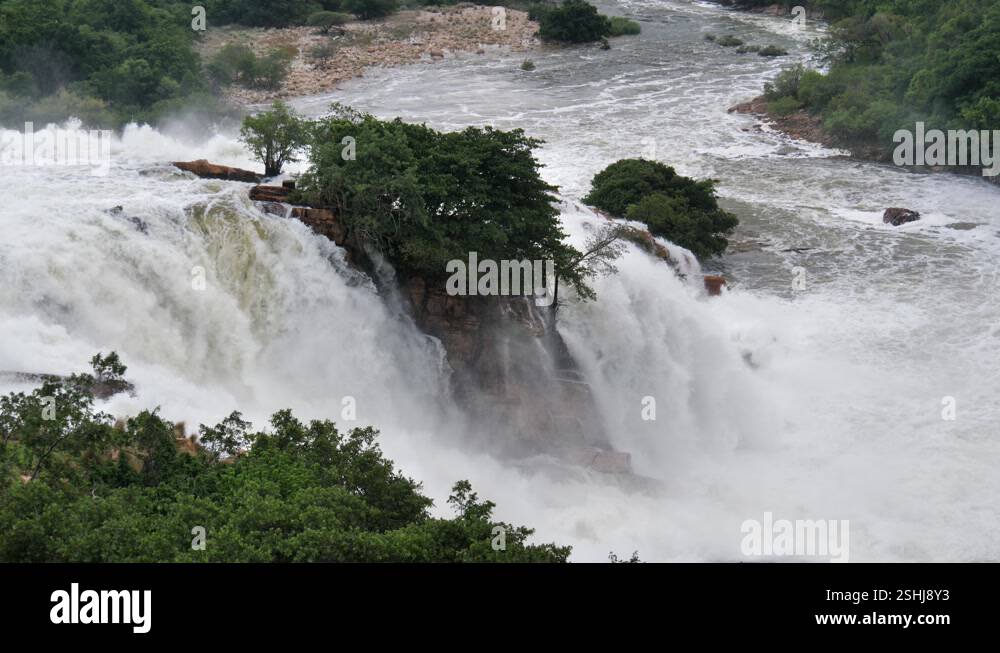 Misty flood water released from power dam flows over rocky waterfall ...