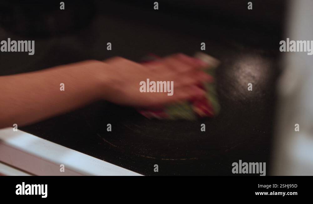 Young South Asian woman's hands wiping down a dirty black stovetop ...