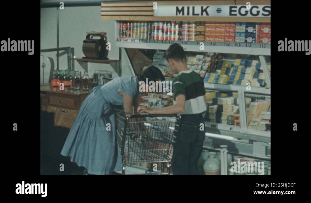 1950s: Woman looks at boxes of fresh vegetables. Woman and boy place ...
