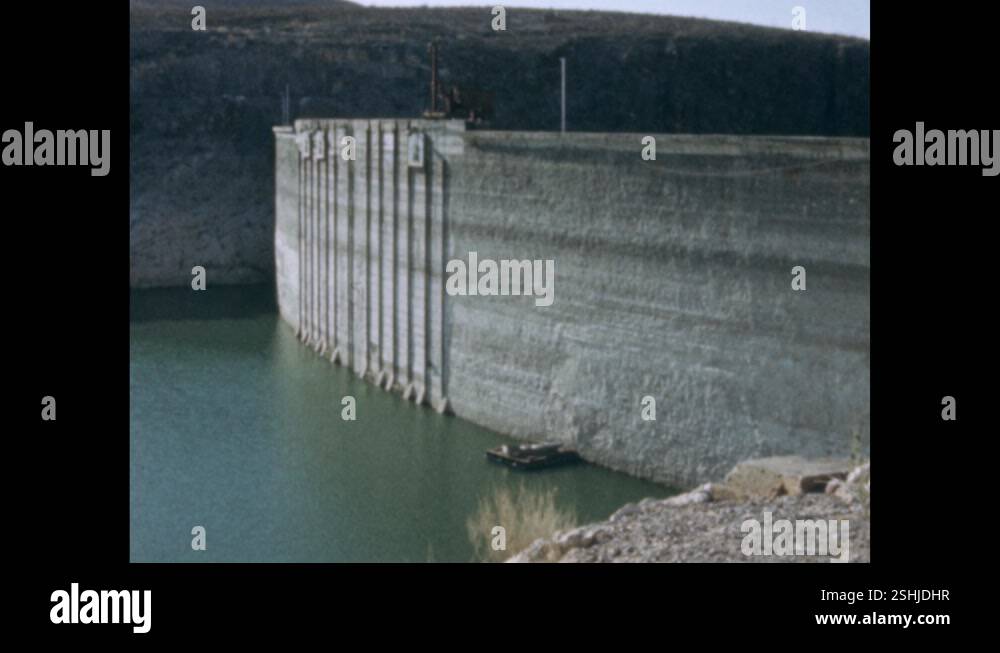 1950s: Hydroelectric dam with boat up against dam. Desert. Three men on ...