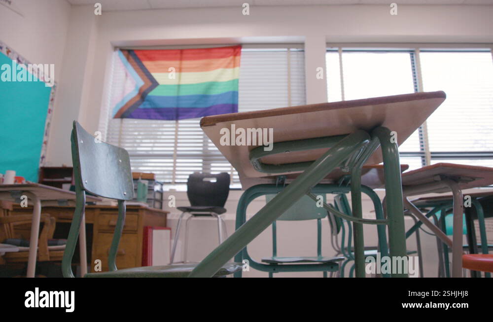 A desk in a classroom with a pride flag on the wall of school learning Stock Video Footage - Alamy