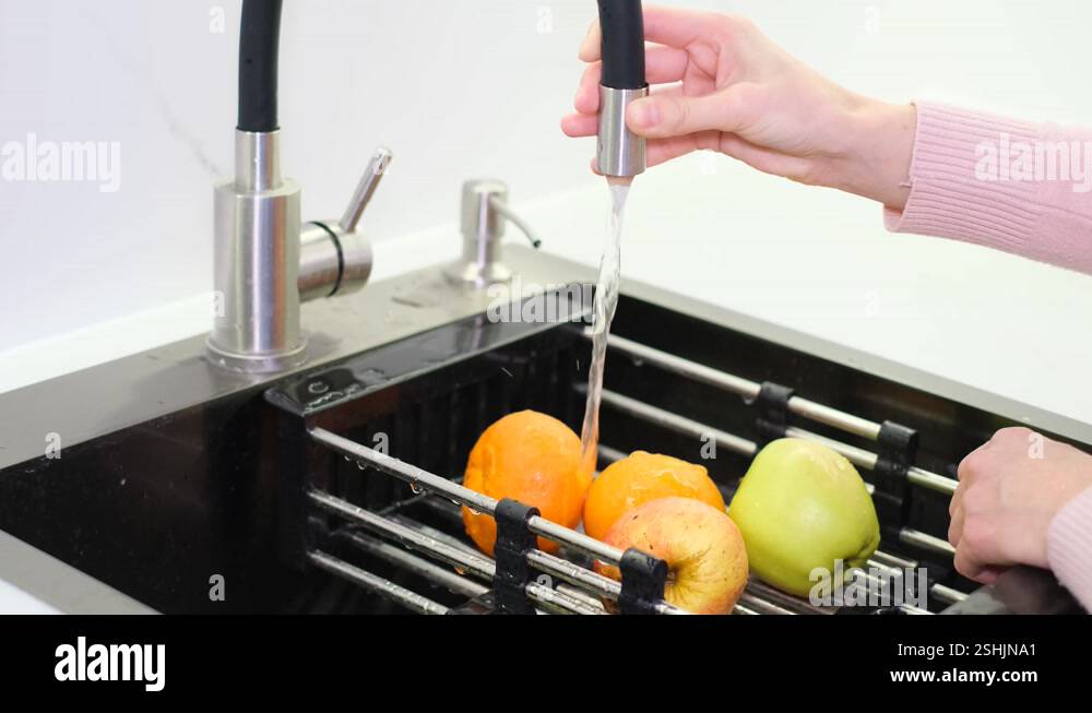Cleaning fresh fruit in the kitchen sink under clean running water ...