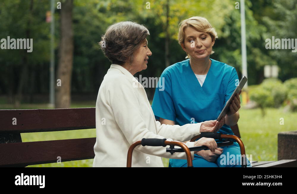 Nurse helping senior woman with disability to make a video call with ...