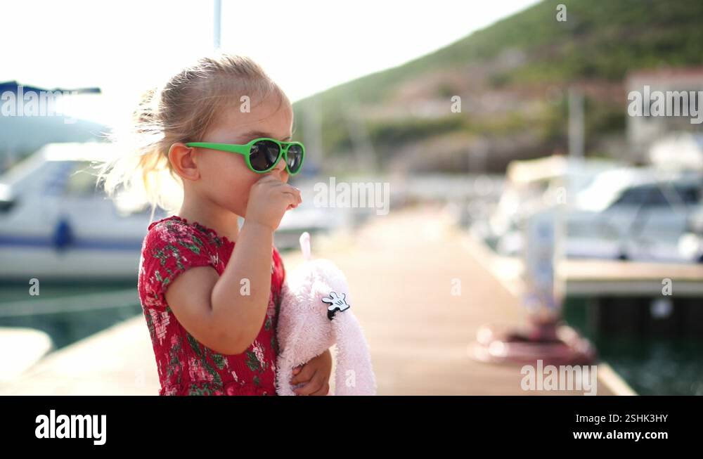 Little girl with a plush hare stands on the pier and eats a bagel Stock ...