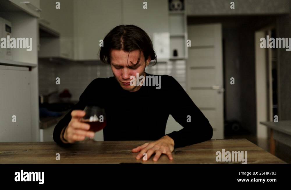 lonely man crying and suffering in the kitchen with a glass of alcohol ...