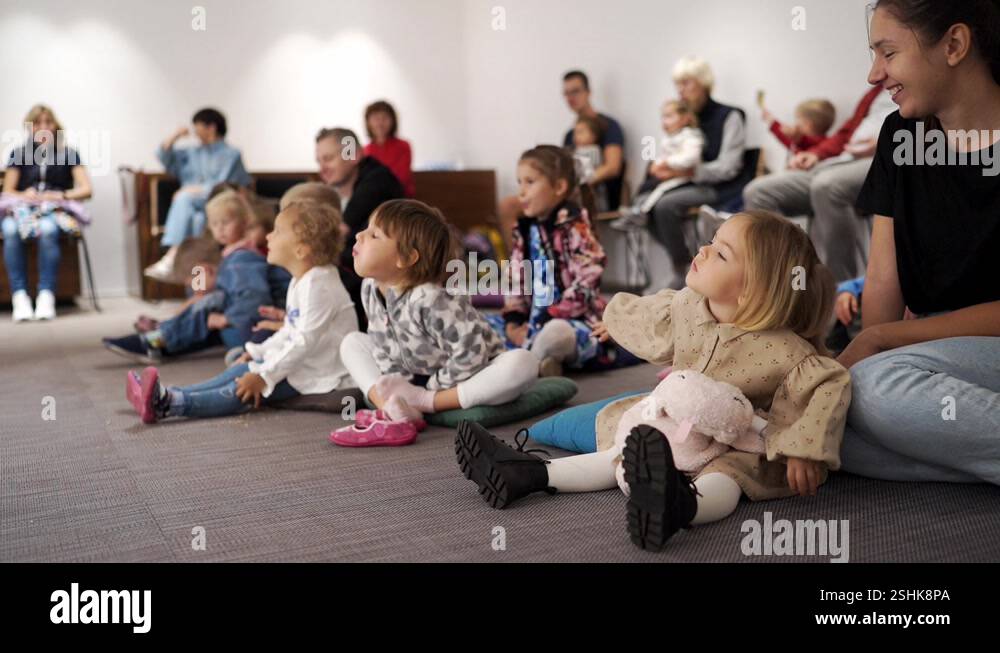 Little children with their parents sit on the floor in the kindergarten ...