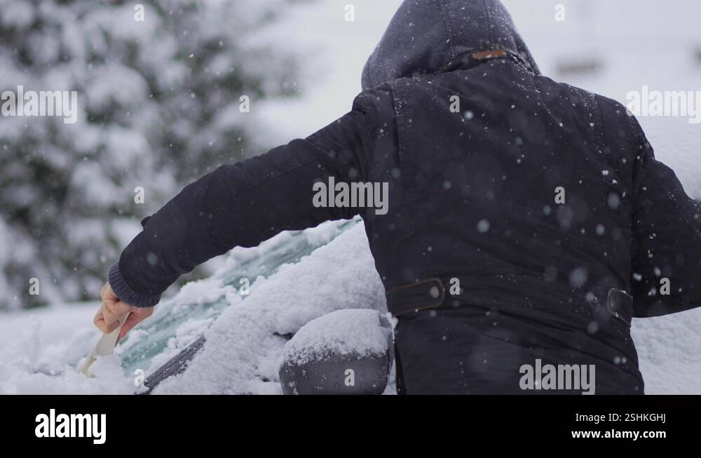 Unrecognizable driver cleaning snow from windshield covered with snow ...