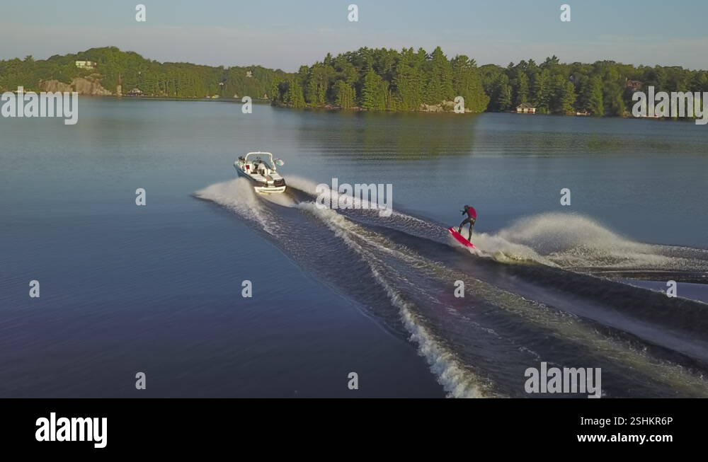 Wake boarder flies like acrobat over motor boat wake wave in calm lake ...