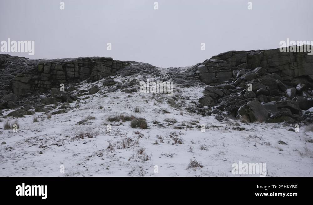 Two men hiking through snow and ice in front of a fallen rock formation ...