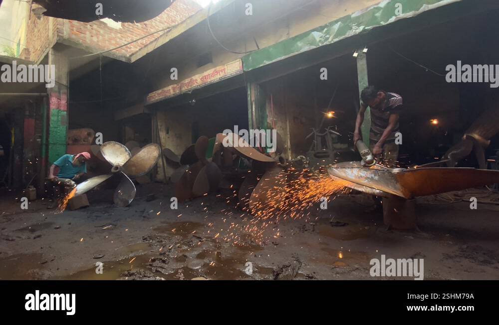 Hand-held shot of men grinding down ship propellers in a workshop in ...