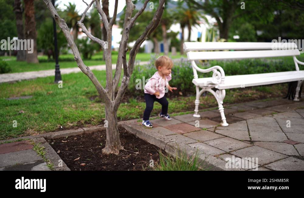 Little girl falls, gets up and walks along the tiles in the park past ...
